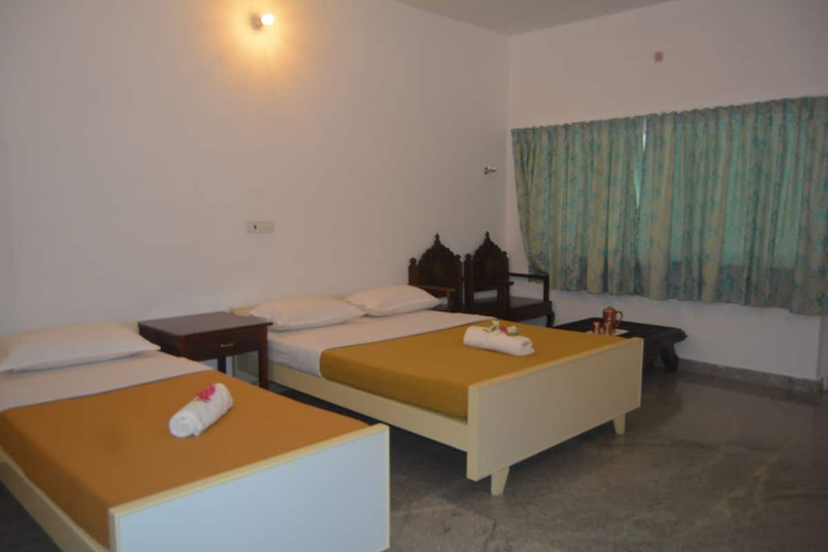 Quarto de hotel com duas camas de solteiro, uma mesa de cabeceira de madeira, uma pequena mesa e uma janela com cortinas.