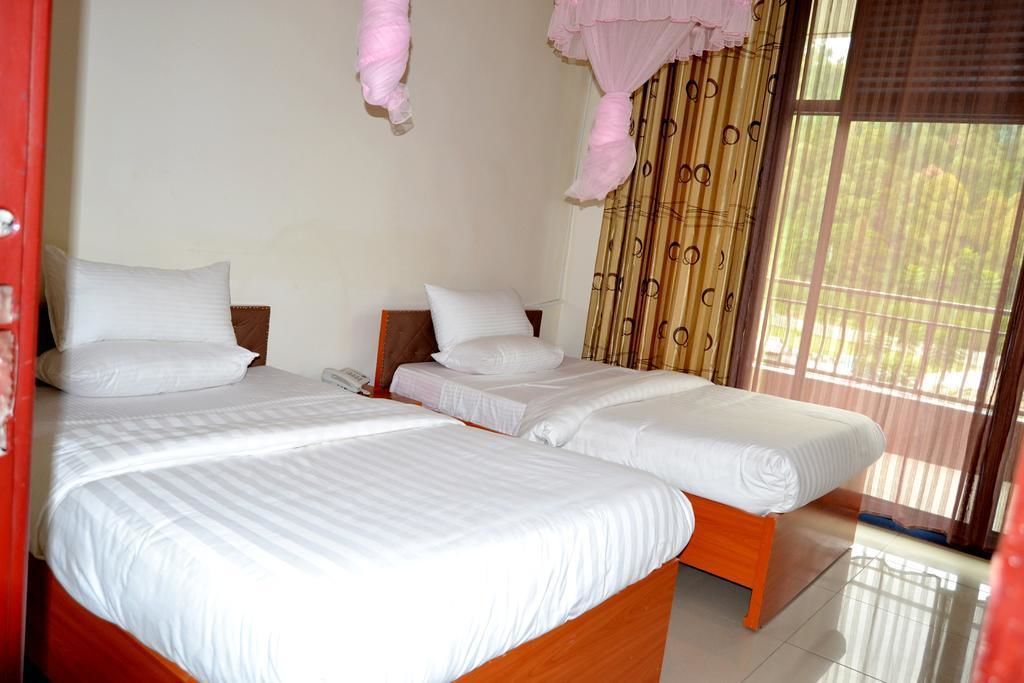 Quarto de hotel com duas camas, cabeceira de madeira, telefone e janela com cortinas.