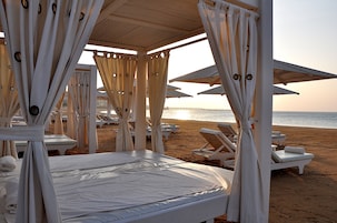 Um hotel à beira-mar com toldos brancos, espreguiçadeiras e uma cama com dossel branco.