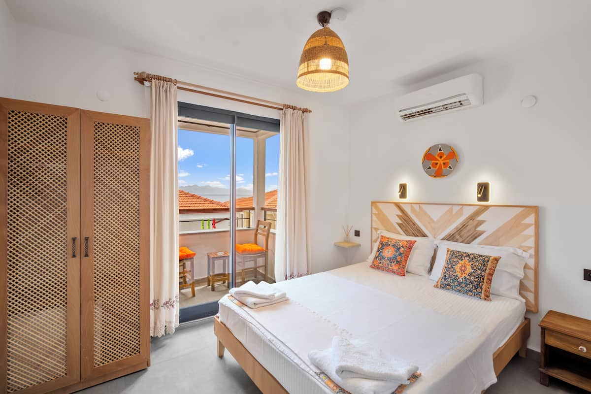 Quarto de hotel com cama, guarda-roupa de madeira, varanda com cadeira e ventoinha no teto.
