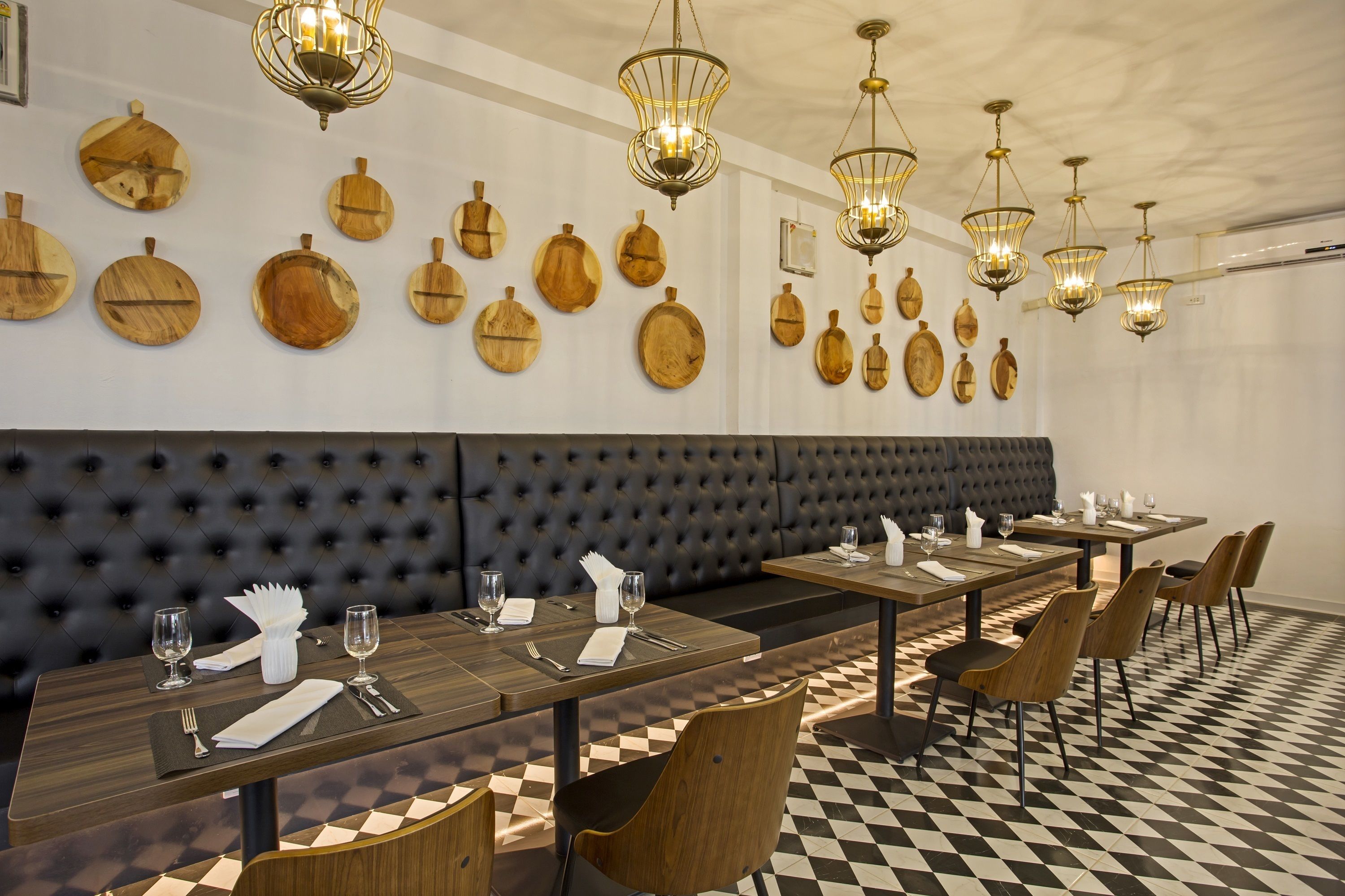 Um restaurante com piso xadrez, mesas de madeira e uma fileira de cabines com encosto estofado.