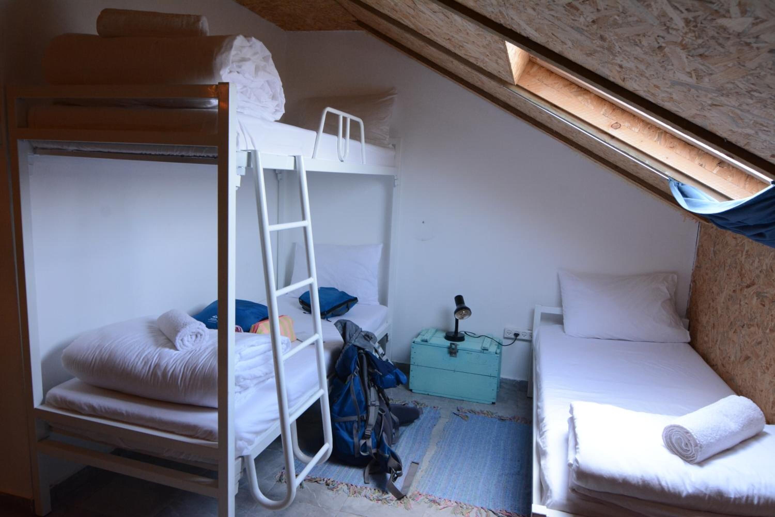 Quarto em dormitório com beliches, escada, pequena escrivaninha e janela.