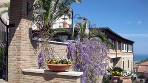 Um edifício com fachada de tijolos, uma varanda com plantas em vasos e vista para o mar.