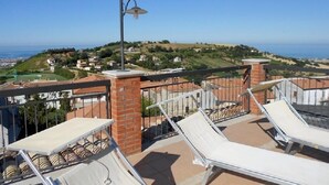 Terraço no telhado com espreguiçadeiras, chaminé de tijolos e um poste de luz.