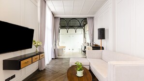Uma sala de estar moderna com televisão de tela plana, mesa de centro de madeira, sofá branco e uma área de jantar ao fundo.