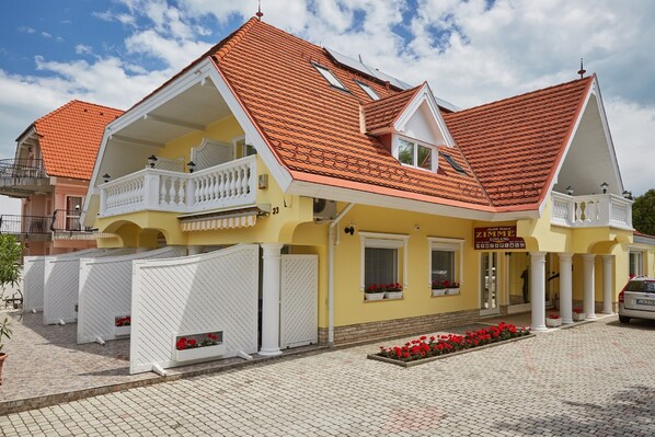 Um edifício amarelo com telhado de telhas vermelhas, varandas brancas e uma placa com a inscrição 'Gold House Zimmerme'.