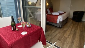 Quarto de hotel com uma cama, uma mesinha com uma garrafa e copos, e vista para o exterior.