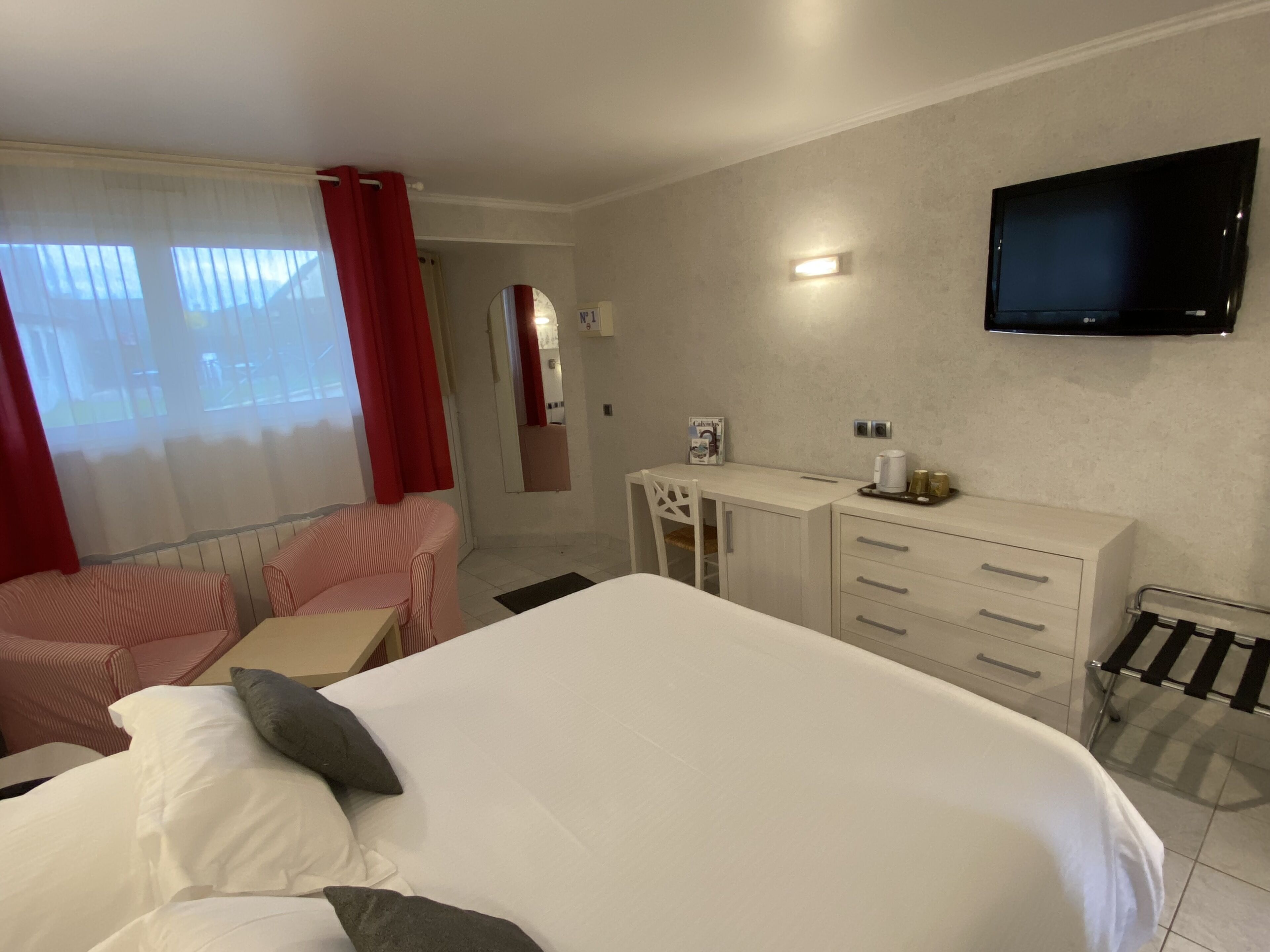 Quarto de hotel com cama, escrivaninha, cadeira, televisão e minibar.