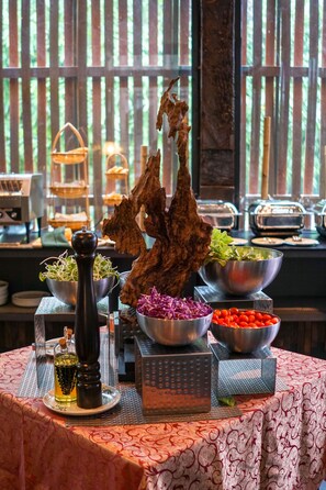 Mesa de buffet com diversos alimentos e acompanhamentos, com um painel de ripas de madeira ao fundo.