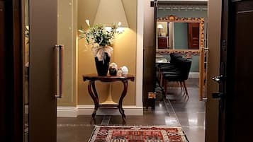 Um corredor com tapete estampado, uma mesa com objetos decorativos e uma luminária.