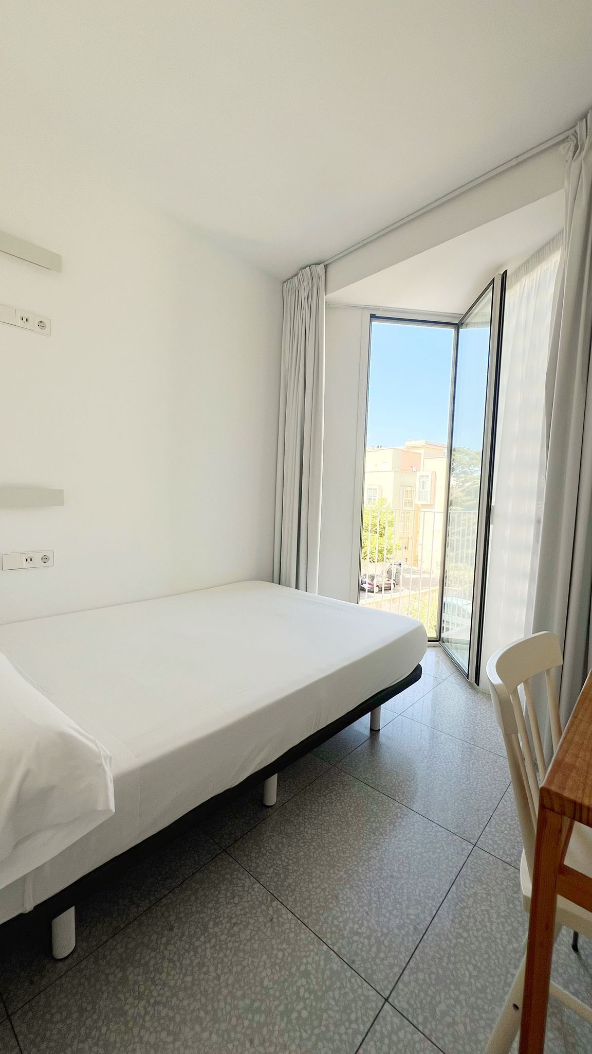 Quarto de hotel com cama, mesa e vista para edifícios através de uma grande janela.