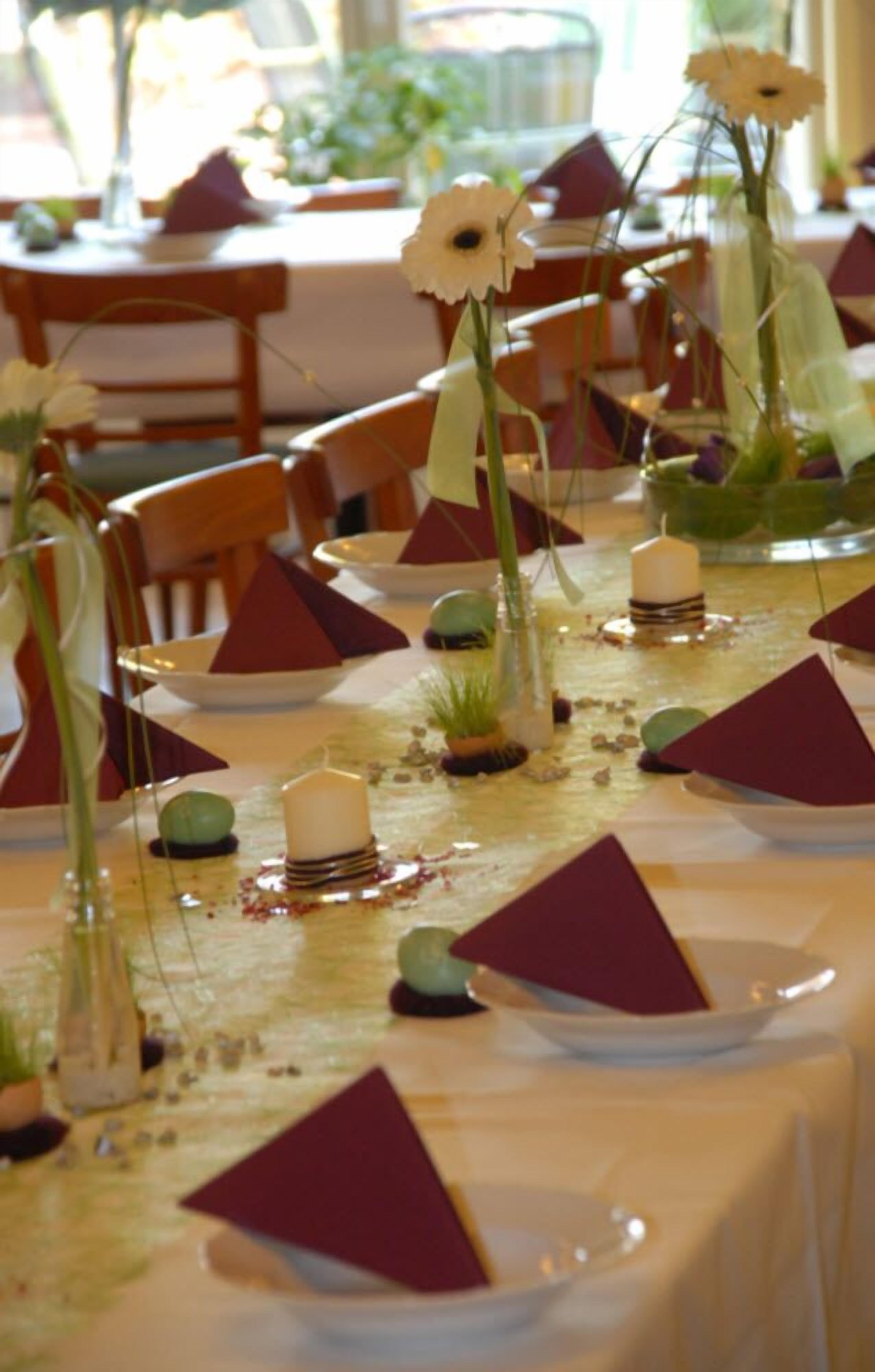 Mesa de jantar posta com guardanapos vermelhos, pratos brancos e centros de mesa florais.