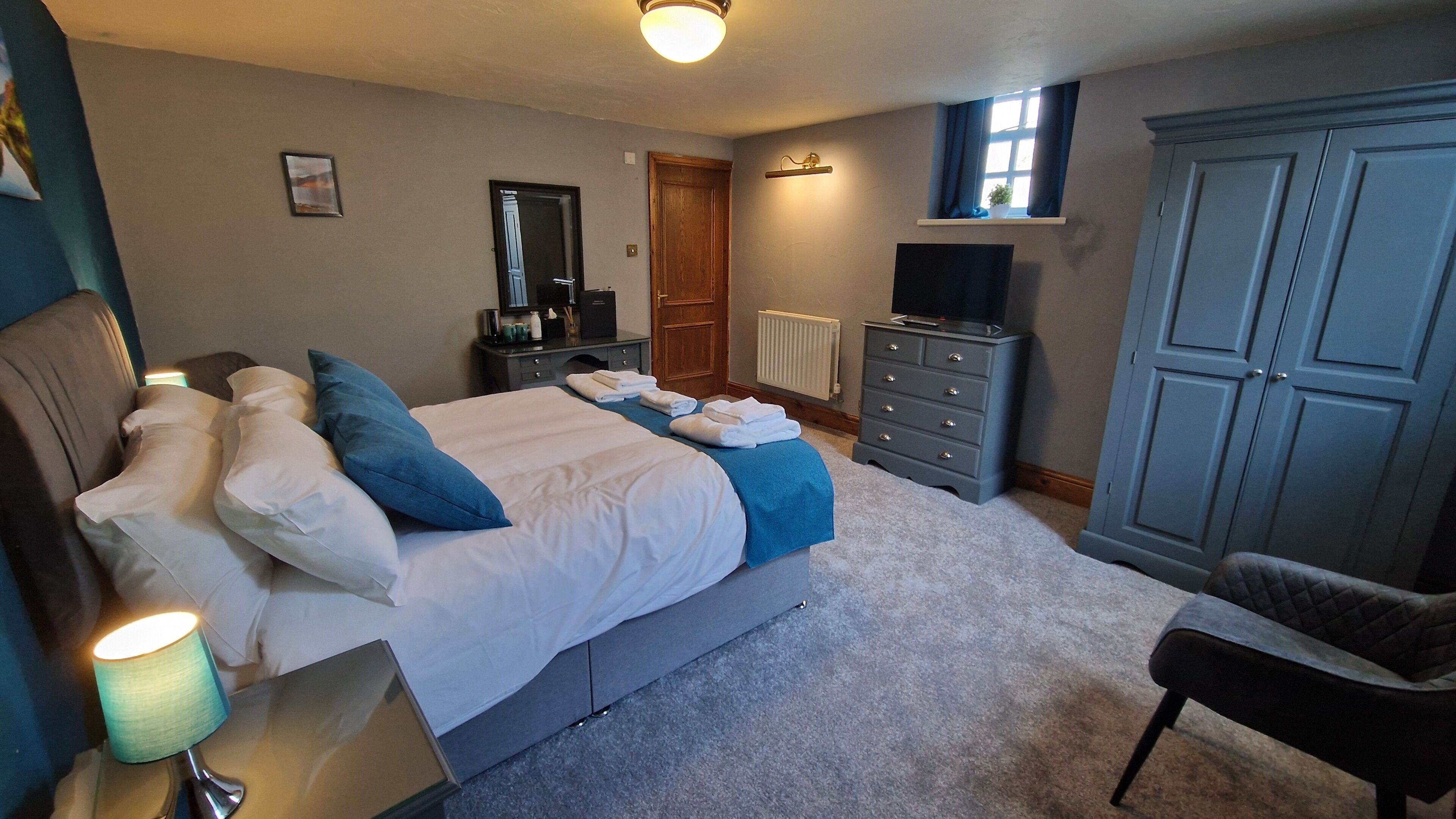 Quarto com cama, penteadeira, cadeira, televisão e janela.