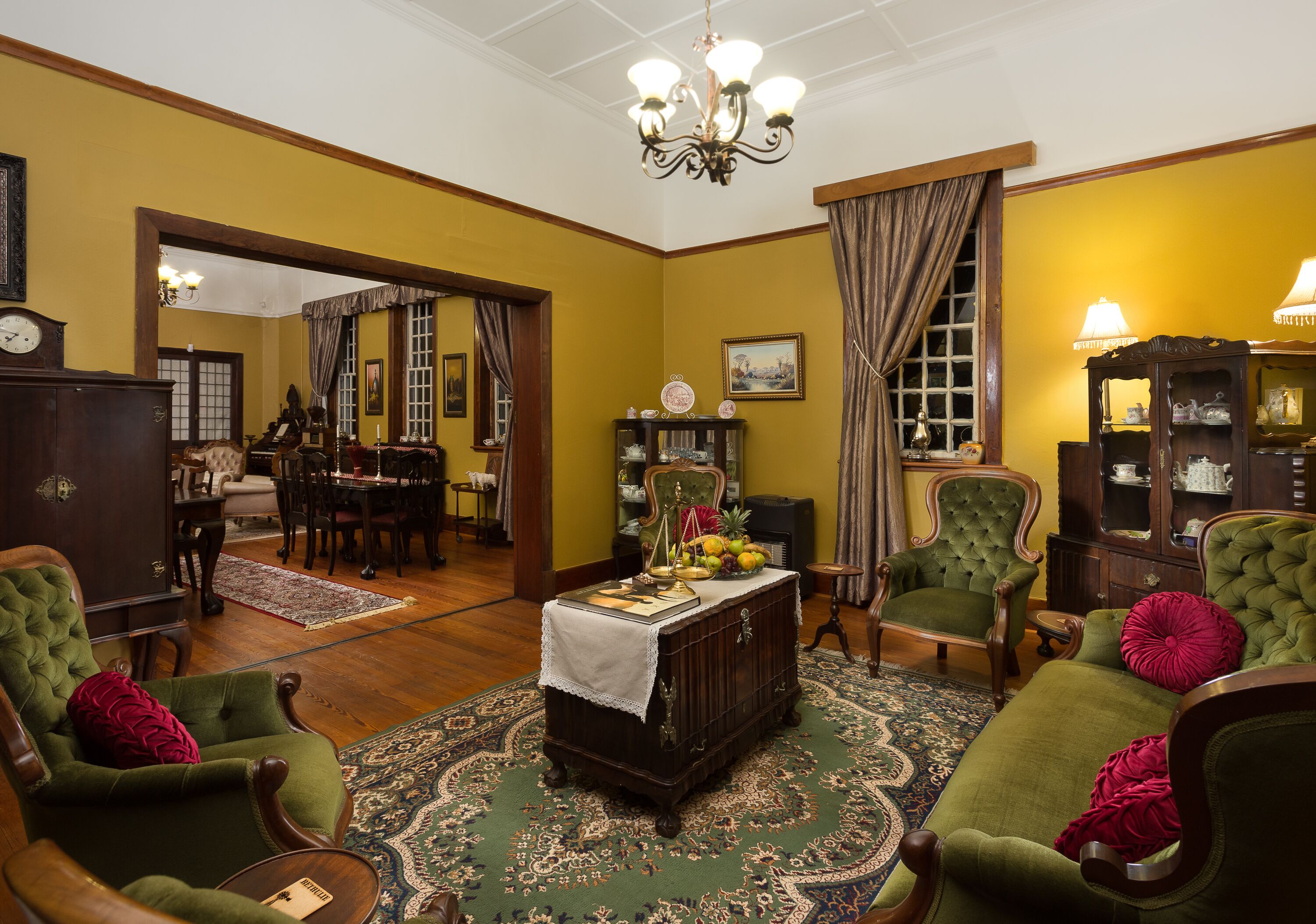 Uma sala de estar tradicional com um sofá verde, poltronas, uma mesa de centro de madeira e um candelabro.