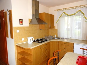 Uma cozinha compacta com armários de madeira, fogão a gás, chaleira e janela com cortina florida.