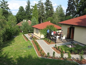 Uma área residencial com uma casa de telhado vermelho, um pequeno jardim com árvores jovens e um caminho de acesso pavimentado.