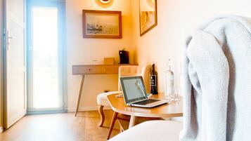 Um quarto aconchegante com um laptop sobre uma mesa de madeira, uma garrafa de vinho e um copo. Há uma cadeira e uma cama com um cobertor.