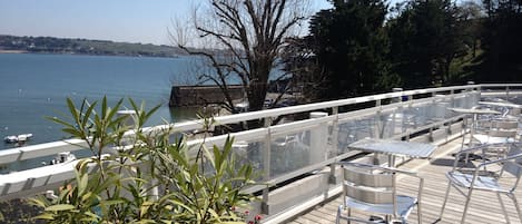 Um terraço com área de estar ao ar livre, vista para um corpo d'água, um vaso de planta e céu claro.