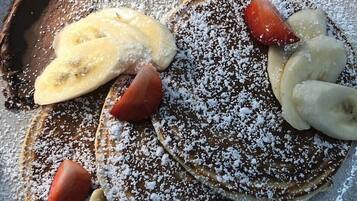 Panquecas com bananas, morangos e açúcar em pó num prato.