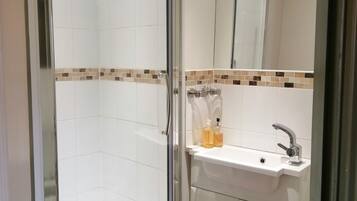 Um banheiro com chuveiro em gabinete de vidro, pia branca com espelho acima e painel de azulejos.