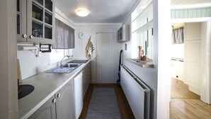 Cozinha estreita com armários brancos, lava-louças embutida e janela com cortinas.