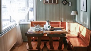 Um quarto aconchegante com uma mesa de madeira, cadeiras, um banco e uma janela com cortinas leves.