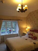 Quarto com cama, janela com cortinas, mesa de cabeceira com abajur e lustre.