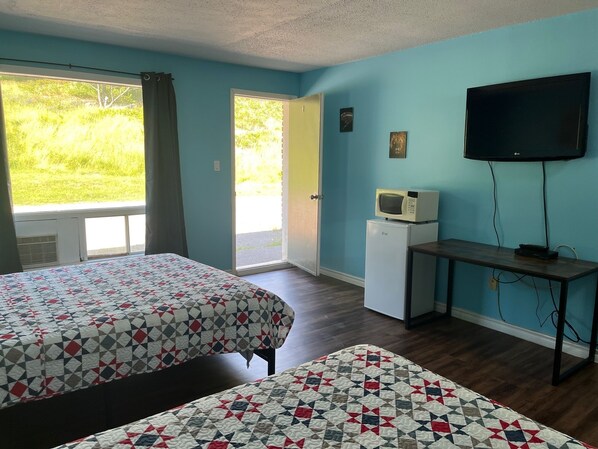 Quarto com duas camas, um refrigerador pequeno, televisão e uma porta que dá para o exterior.