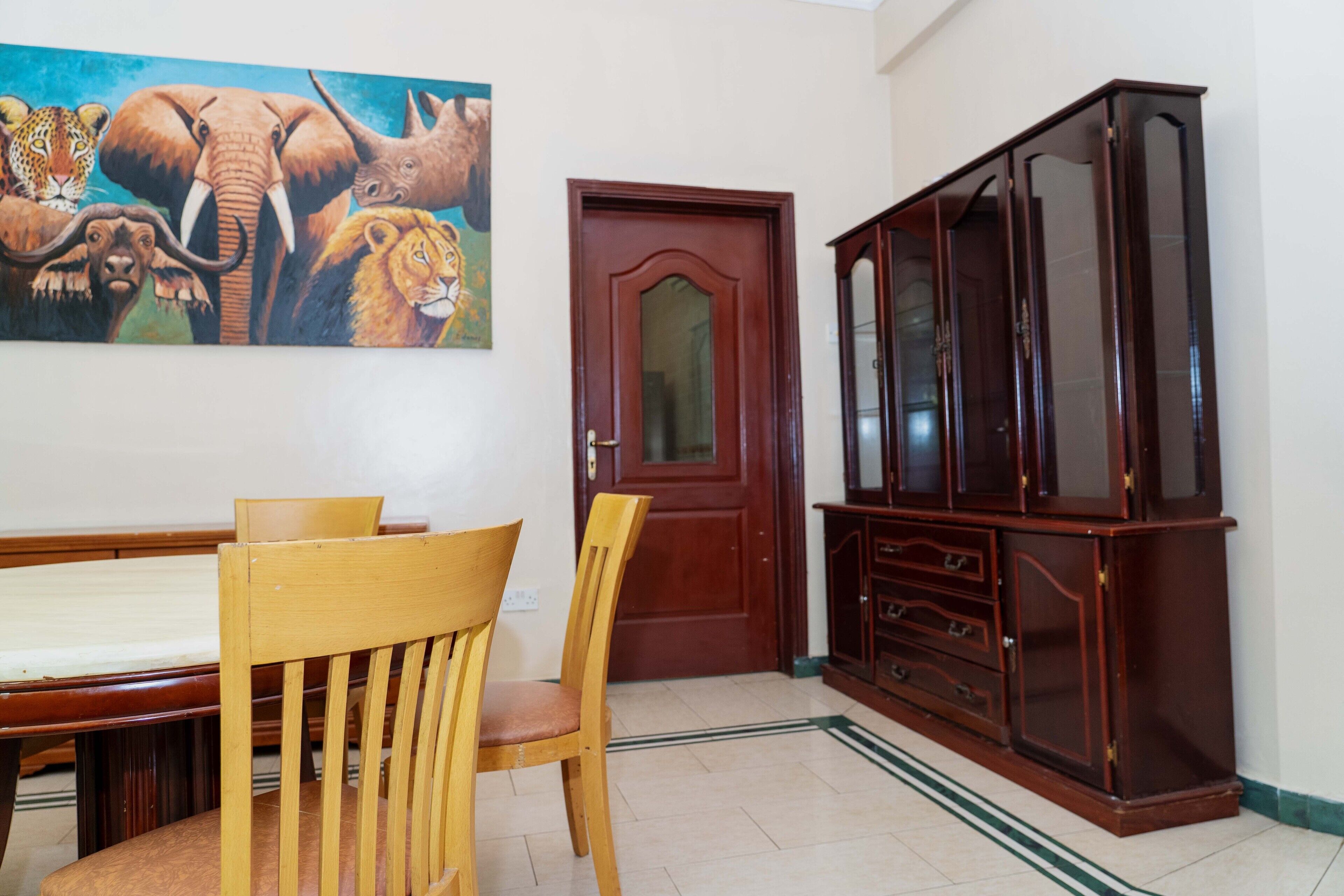 Uma sala de jantar com uma mesa e cadeiras de madeira, um armário de madeira e um quadro com animais na parede.