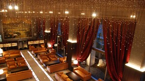 Um saguão de hotel com diversas áreas de estar, um lustre grande e cortinas vermelhas.