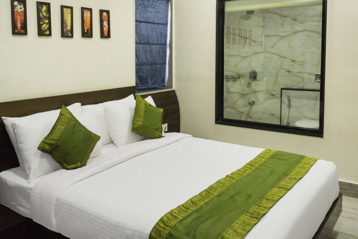 Uma cama bem arrumada com roupa de cama branca e almofadas verdes, parede com padrão marmorizado e uma coleção de obras de arte emolduradas acima da cama.