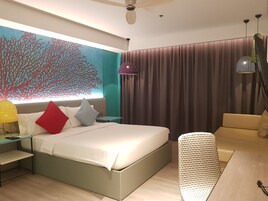 Quarto de hotel moderno com uma cama grande, uma mesinha de cabeceira, um sofá, parede decorativa e um ventilador de teto.