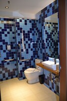 Casa de banho com azulejos azuis, sanita branca, lavatório e chuveiro.