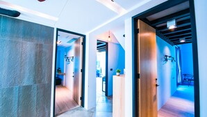Corredor moderno com porta de madeira, parede revestida de azulejos e um quarto iluminado em azul ao fundo.