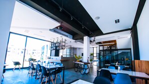 Um restaurante moderno com pé-direito alto, amplas janelas e uma variedade de arranjos de assentos, incluindo mesas e cadeiras.