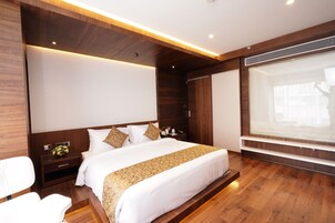 Quarto de hotel moderno com uma cama grande, piso de madeira, mesa de cabeceira com um vaso de flores e uma janela ampla com vista.