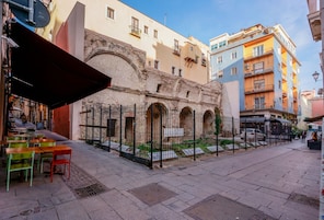 Pátio com mesas ao ar livre, uma fonte e edifícios com varandas.
