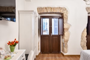 Um quarto com um arco de pedra que leva a uma porta, um aparador branco com um vaso de tulipas e uma televisão de tela plana presa na parede.
