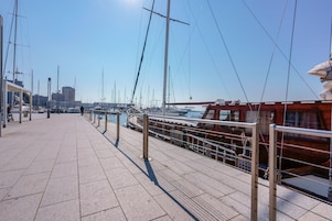 Marina com barcos atracados, céu claro e um calçadão calçado.