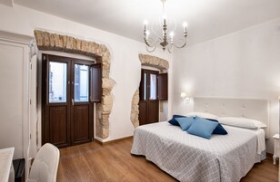 Quarto com cama grande, paredes de pedra, portas de madeira e um candelabro.