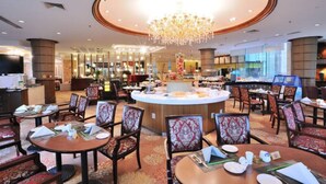 Um saguão de hotel com mesas redondas, cadeiras, área de bar central e um candelabro.