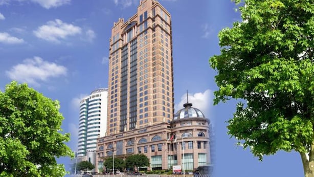 Um edifício alto com estilo arquitetônico clássico, cercado por árvores verdes exuberantes.