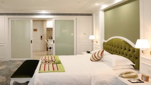 Quarto de hotel com cama, um banco, uma TV e uma porta que dá para o banheiro.