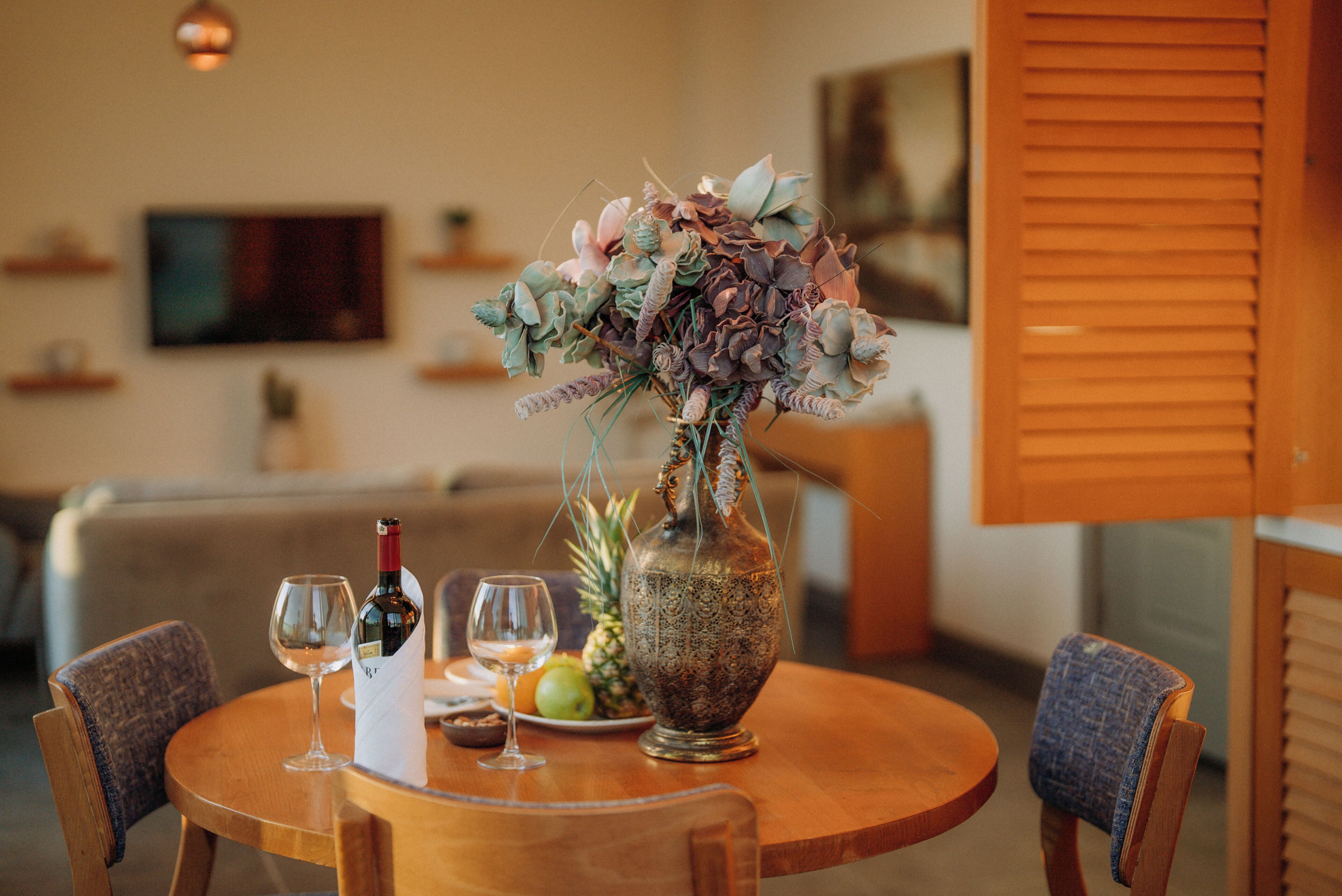 Uma mesa redonda de madeira com um vaso de flores, uma garrafa de vinho e uma abacaxi.