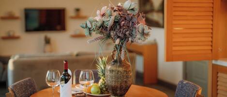 Uma mesa redonda de madeira com um vaso de flores, uma garrafa de vinho e uma abacaxi.