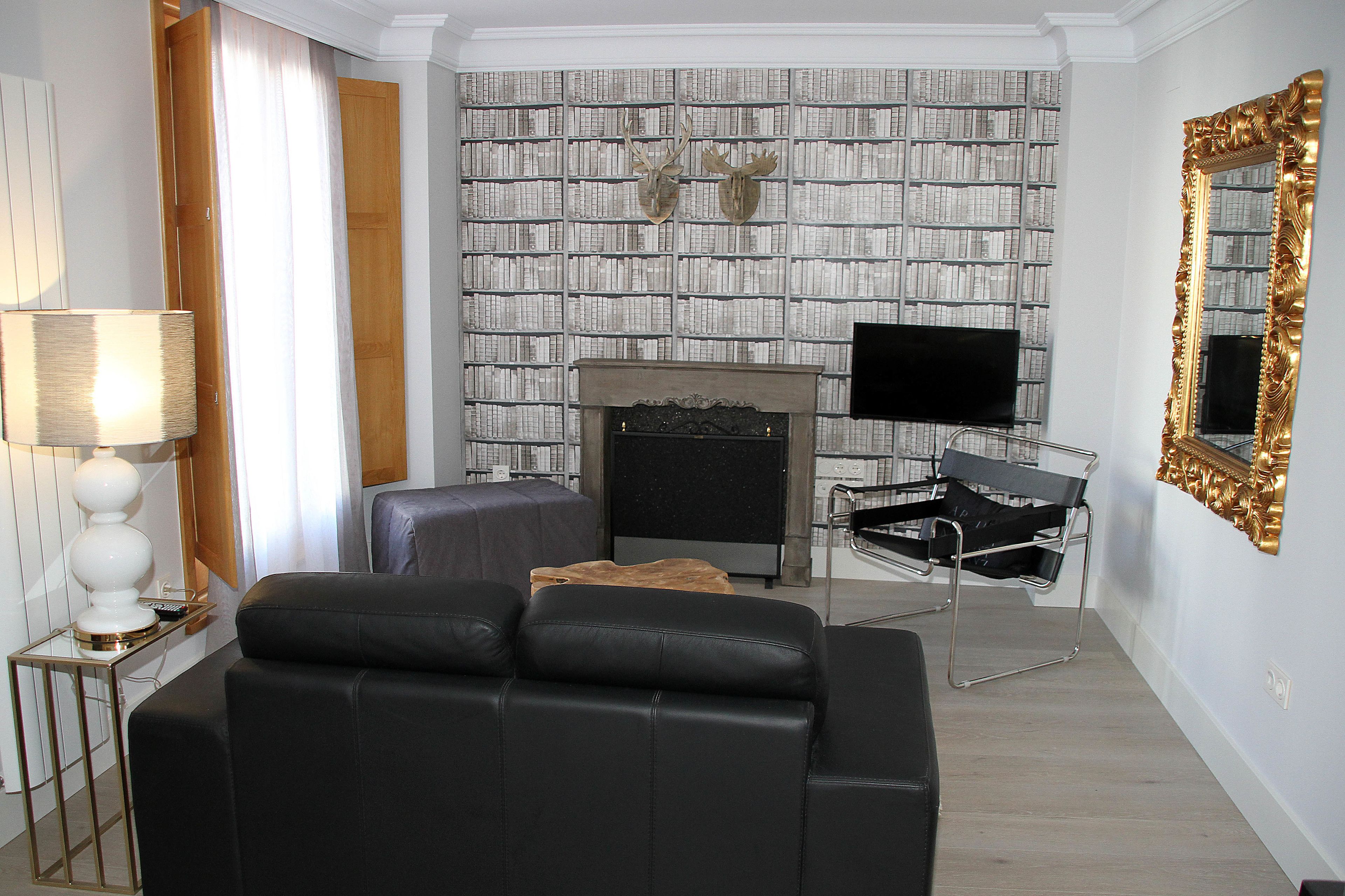 Uma sala de estar moderna com lareira, um sofá de couro preto, uma parede com estantes e um espelho grande.