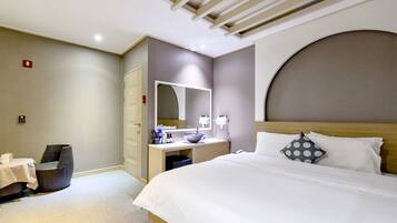 Quarto de hotel com cama, escrivaninha com espelho, cadeira e uma pequena mesa com uma xícara.