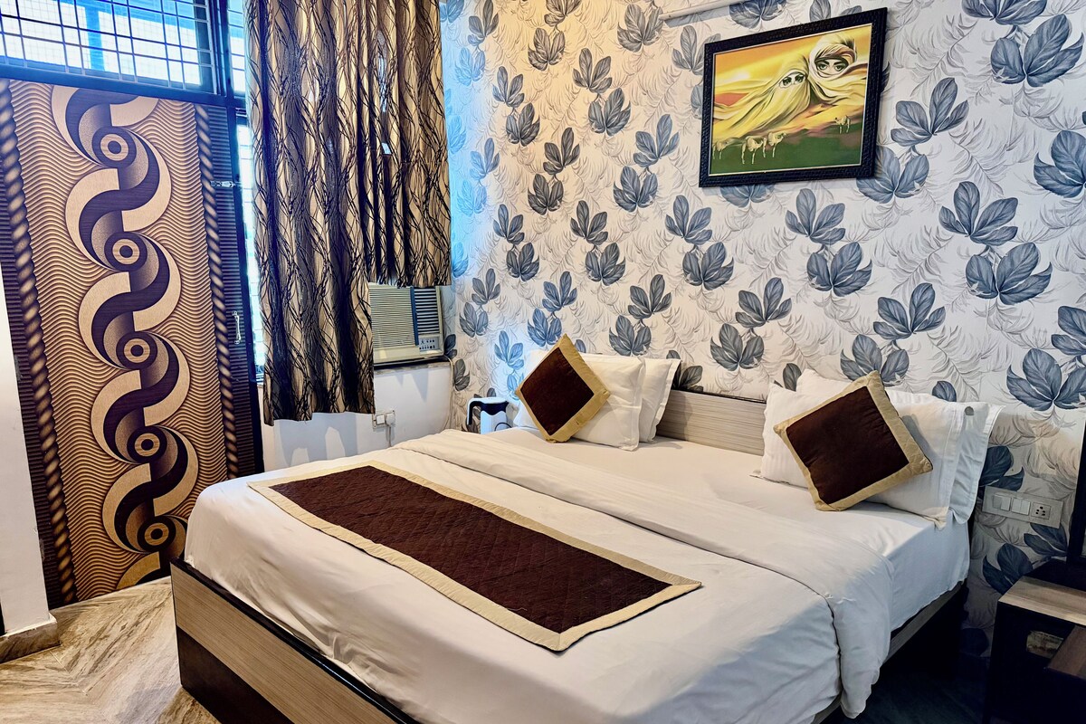 Quarto de hotel com cama, mesa de cabeceira, ar condicionado fixado na parede e janela com cortinas.