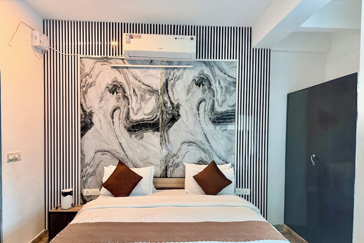 Quarto de hotel com cama grande, cabeceira com padrão de mármore, guarda-roupa e ar condicionado.