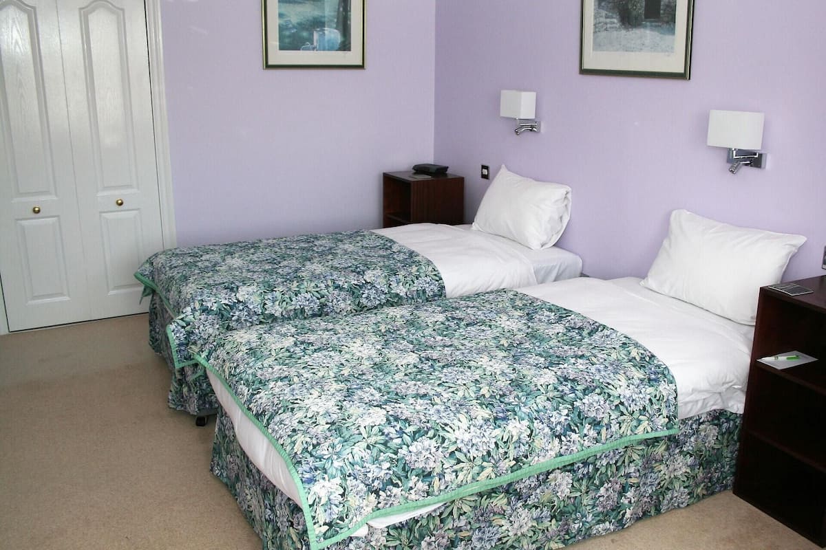 Quarto com duas camas, colchas floridas, uma porta branca e duas fotos emolduradas na parede.